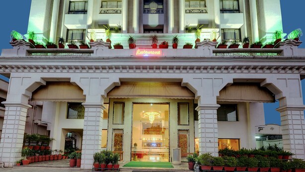 Hotel com design arquitetônico clássico, apresentando uma entrada imponente com fachada de vidro ampla e uma placa de neon acima da entrada.