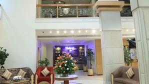 Um hall espaçoso com um lustre imponente, várias áreas de estar e um arranjo floral central.
