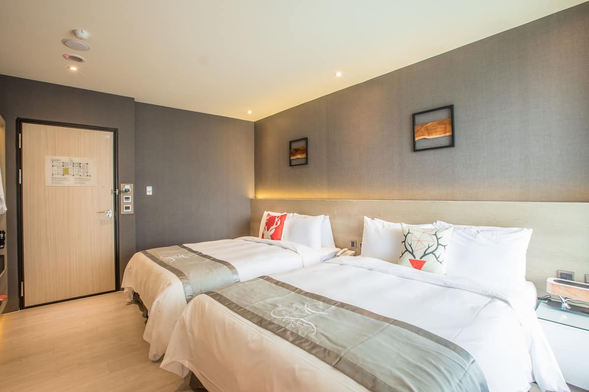 Quarto de hotel com duas camas, uma porta de madeira e um quadro emoldurado na parede.