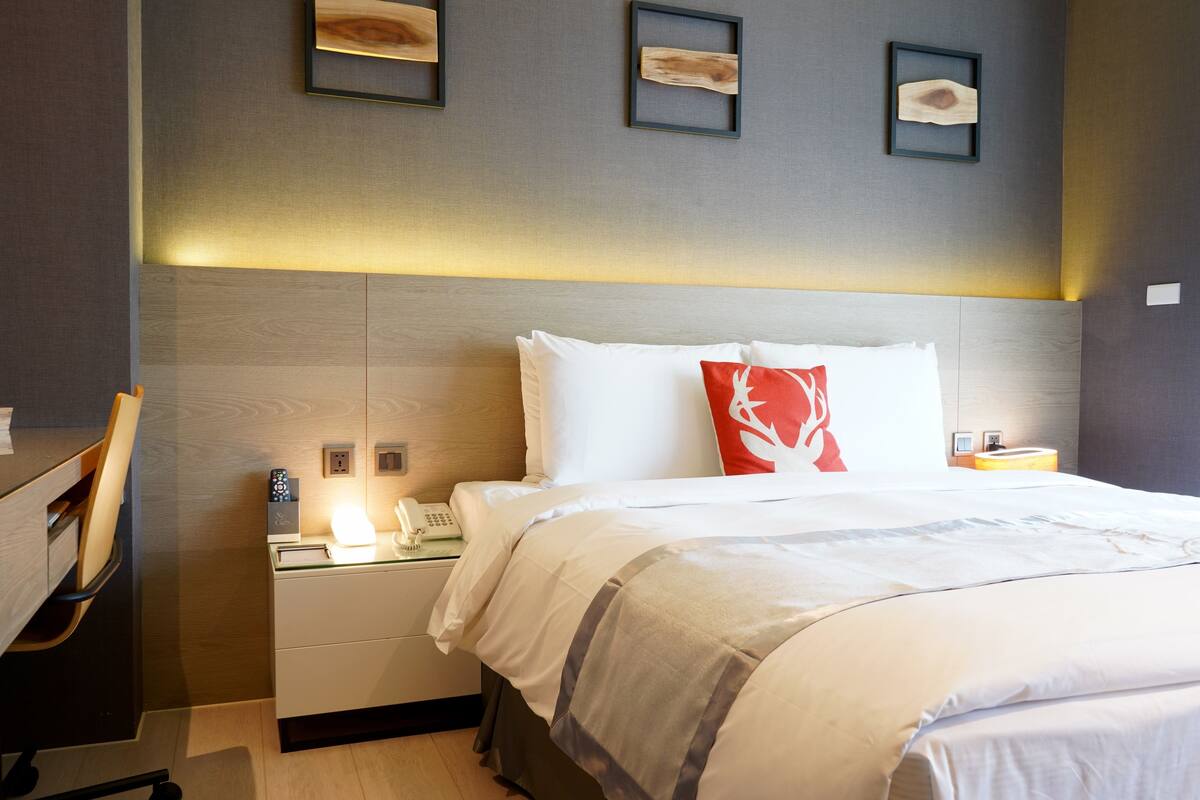 Quarto de hotel com uma cama bem arrumada, mesas de cabeceira e um telefone fixado na parede.