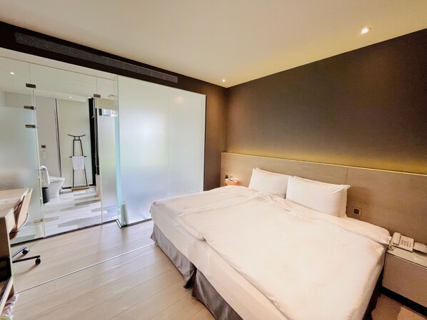 Quarto de hotel moderno com uma cama grande, telefone ao lado da cama e área de chuveiro com paredes de vidro.