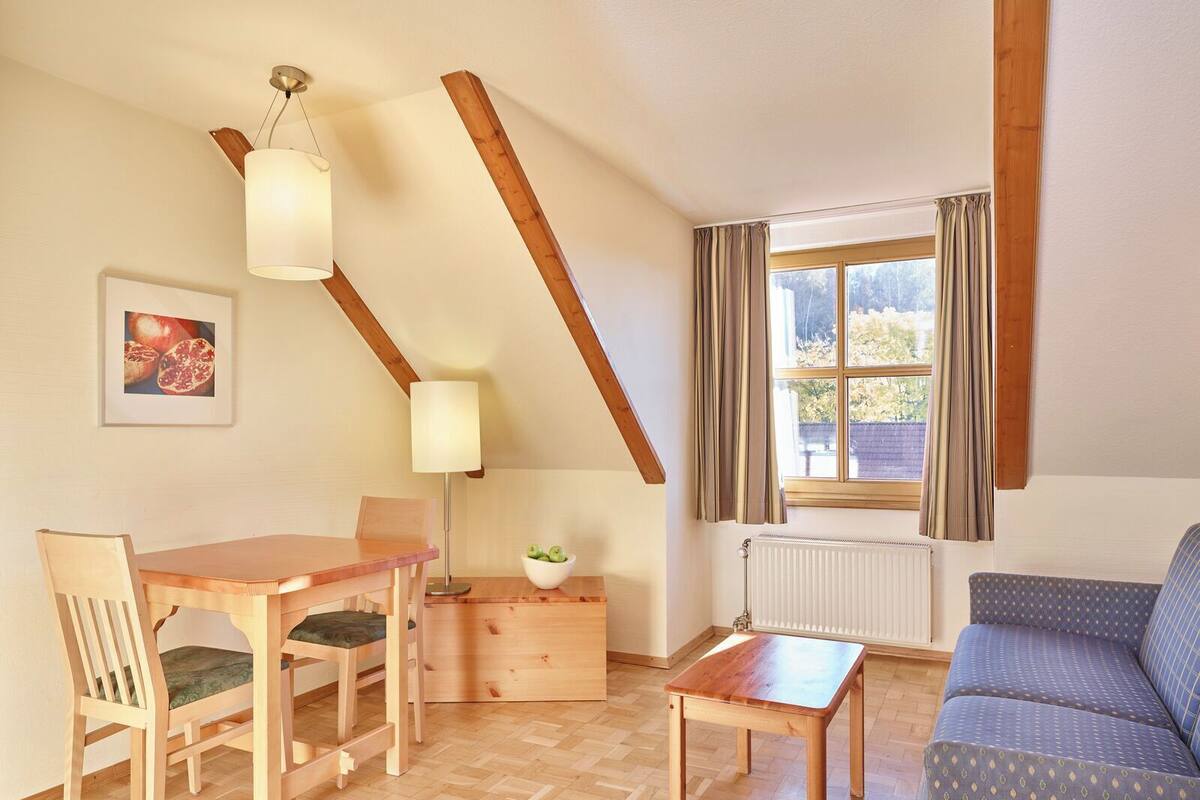 Um quarto aconchegante com uma mesa de jantar de madeira, duas cadeiras, um sofá e uma janela com cortinas.