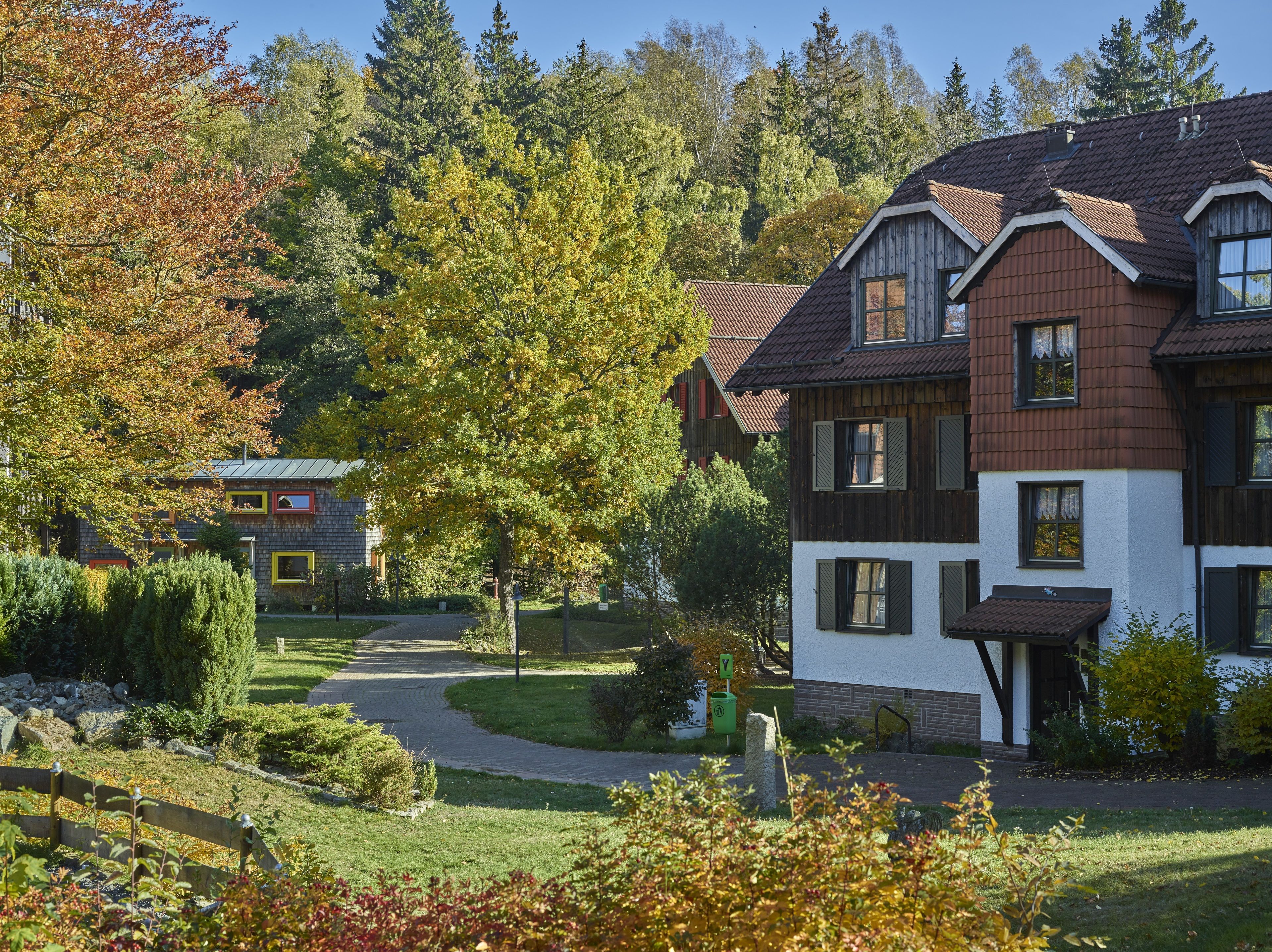 Um edifício em estilo europeu tradicional, com telhado inclinado e várias janelas, rodeado por um jardim bem cuidado e árvores.