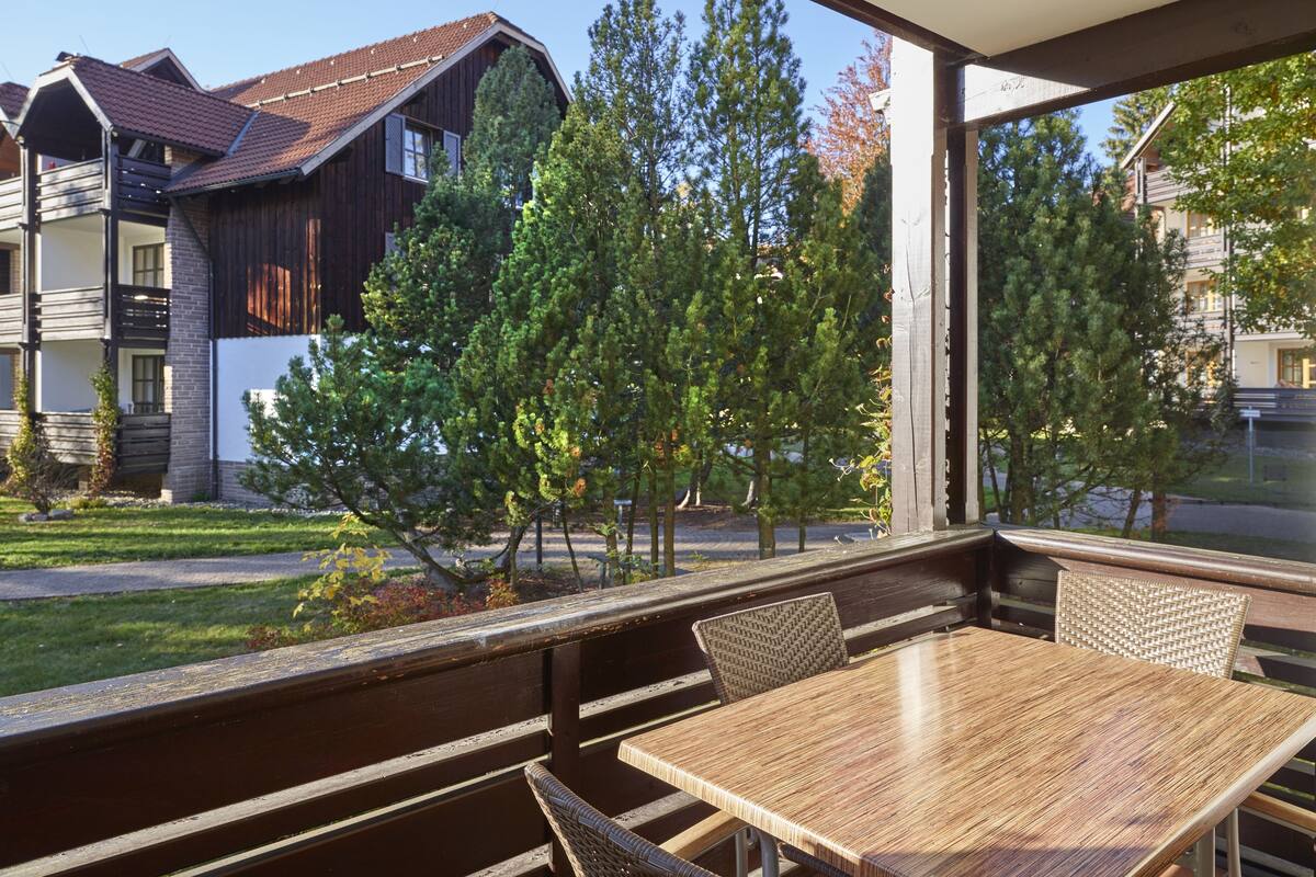 Varanda com mesa e cadeiras, vista para área residencial com casas e árvores.