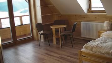 Quarto aconchegante com piso de madeira, uma cama, uma mesa com cadeiras e janela com vista para uma paisagem coberta de neve.