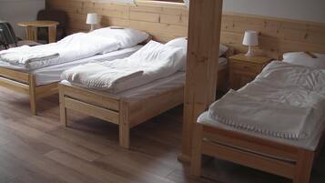 Quarto com três camas de madeira, uma mesinha e uma cadeira.