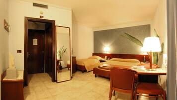 Quarto de hotel com uma cama, uma escrivaninha com cadeira, um espelho e uma luminária.