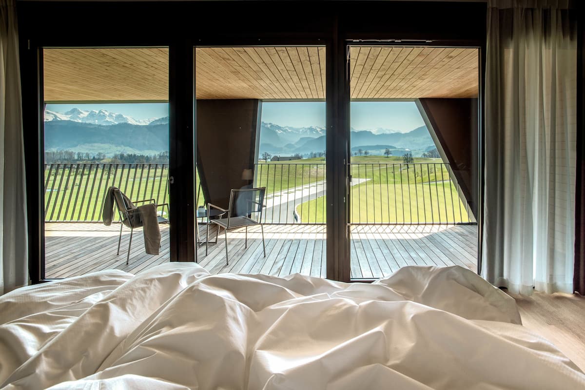 Quarto com uma cama grande e vista para uma varanda com cadeira e mesa.