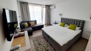 Quarto de hotel moderno com uma cama grande, um sofá, uma TV e uma janela com cortinas.