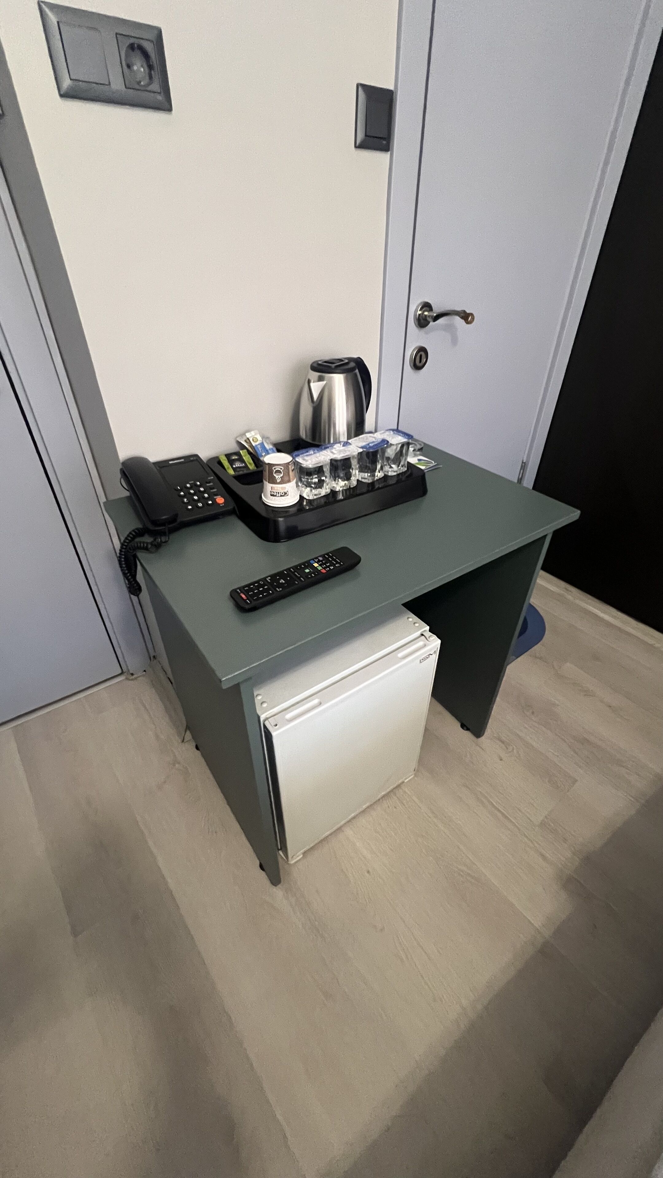 Uma pequena cozinha compacta com cafeteira, chaleira, micro-ondas e geladeira.