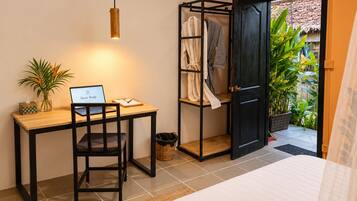 Quarto com cama, escrivaninha com laptop, cadeira, mesinha com planta, guarda-roupa preto e porta que dá para um jardim.
