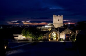 Um edifício histórico com uma torre, entrada em arco e janelas iluminadas à noite.