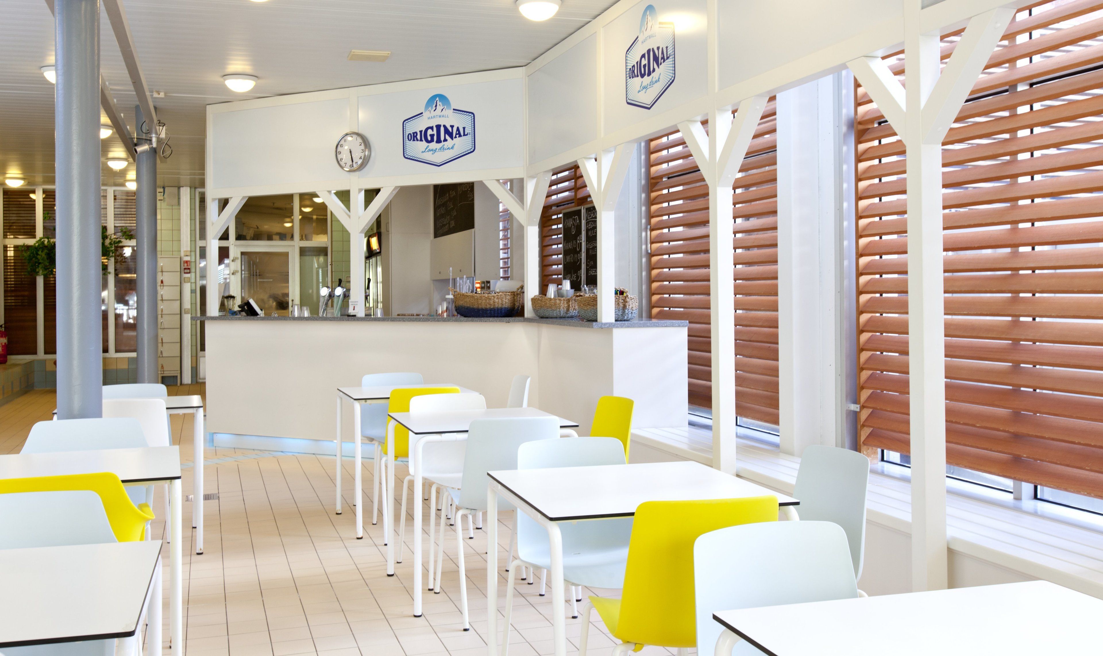 Interior de restaurante com cadeiras e mesas brancas e amarelas, e um quadro de menu visível.