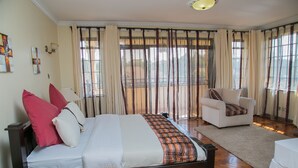 Quarto com uma cama grande, uma poltrona branca e vista para o exterior através de cortinas.