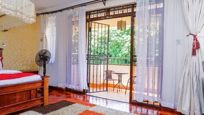 Quarto com cama, ventilador, tapete estampado e vista para uma varanda com portão.