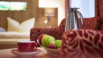 Quarto de hotel com uma mesa de jantar posta com uma xícara vermelha, uma tigela de frutas e um jarro de café prateado.