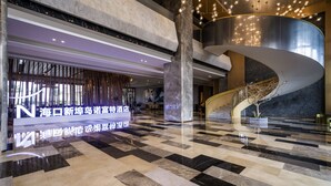 Um hall de hotel moderno com piso xadrez, um pilar grande e uma escadaria curva.