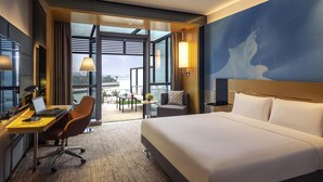 Quarto de hotel com cama, escrivaninha, cadeira e vista para o exterior.