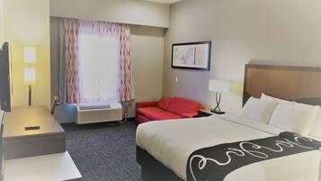 Quarto de hotel com cama, escrivaninha, cadeira, televisão, luminária, janela com cortinas e um quadro na parede.