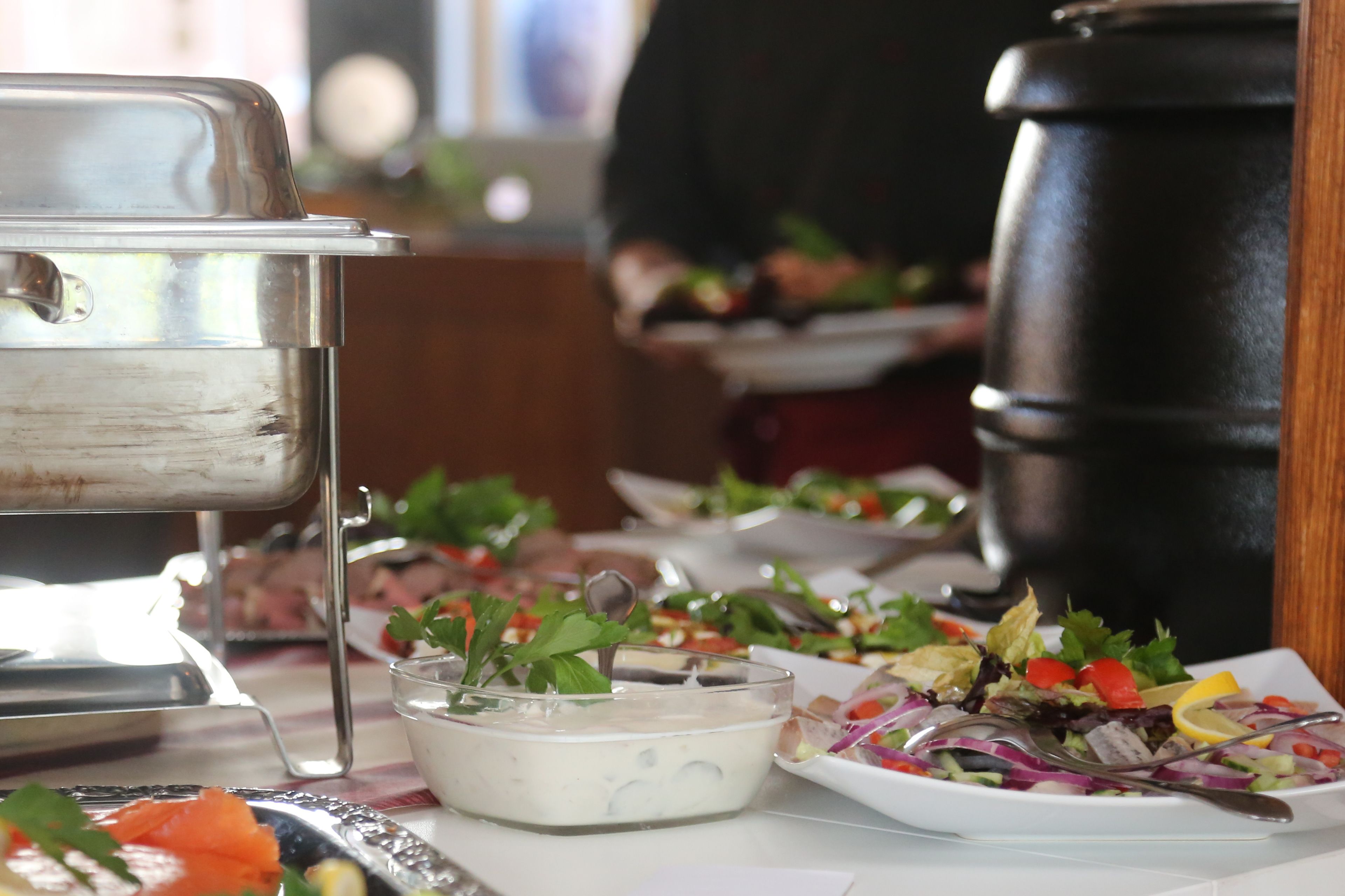 Mesa de buffet com diversos pratos, incluindo uma salada, um creme para molhar e um prato com legumes e carne.