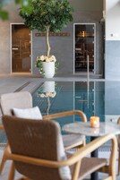 Uma área interna de piscina moderna, com assentos e uma grande árvore em vaso.