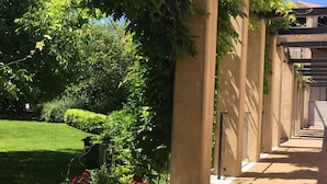Uma galeria coberta com piso de azulejos, rodeada por vegetação e plantas em vasos.