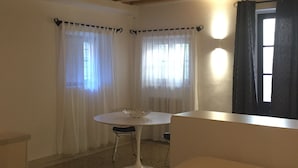 Um quarto com uma mesa e cadeira brancas, um sofá branco e uma janela com cortinas.