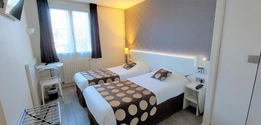 Quarto de hotel com duas camas, um radiador, uma mesa pequena e televisão presa à parede.