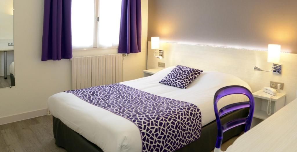 Quarto de hotel com cama, duas luminárias de cabeceira, uma cadeira e janela com cortinas.