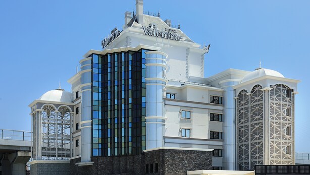 Um hotel com design arquitetônico moderno, destacando uma torre imponente com o nome 'Valentine' e uma grande fachada de vidro.