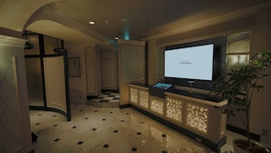 Uma área de recepção de hotel com um painel digital, balcão de check-in e piso xadrez.