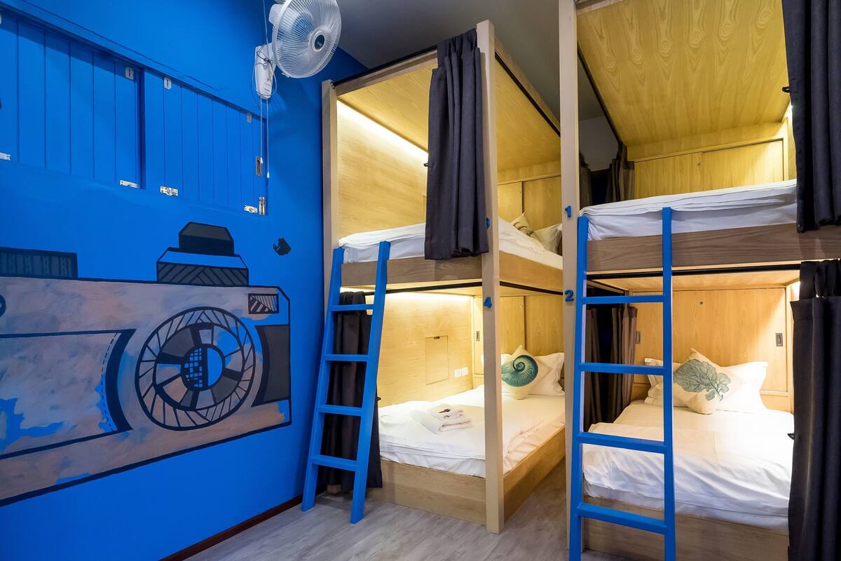 Quarto com beliches, um ventilador e um mural na parede.