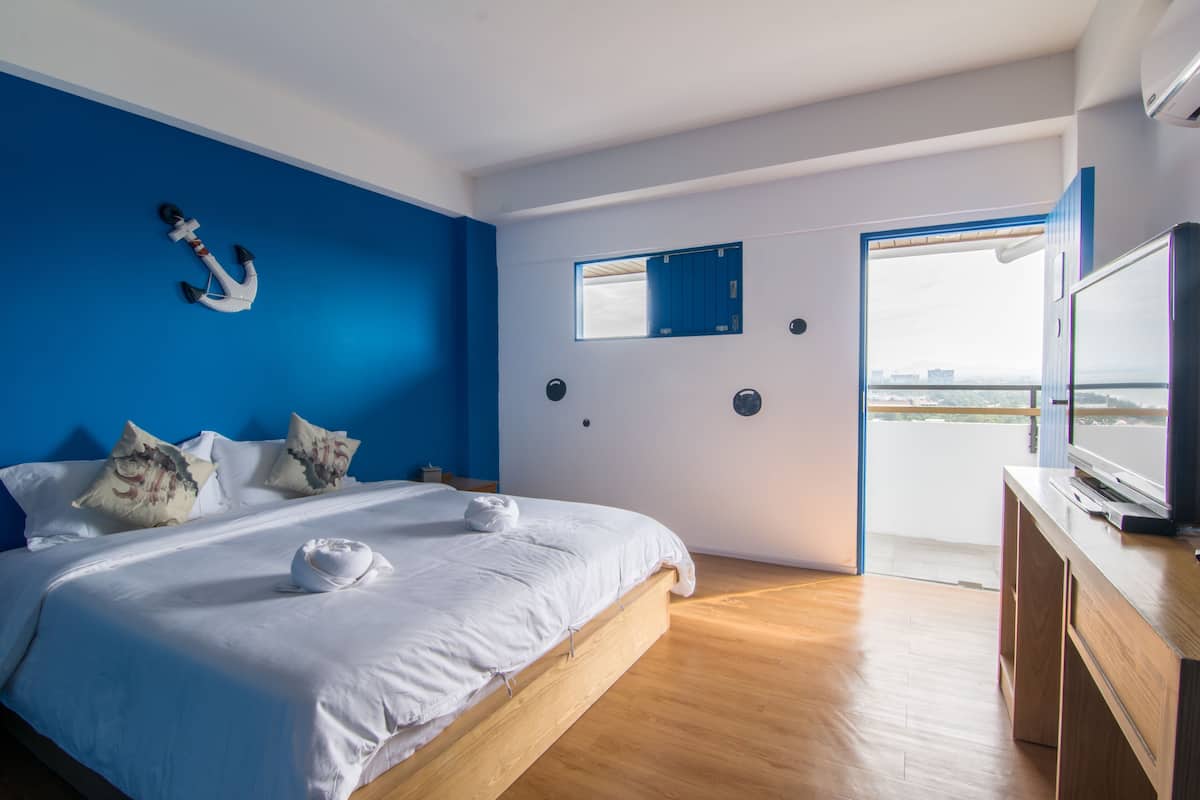 Quarto moderno com cama, cómoda de madeira, televisão e vista para a cidade através de uma janela.