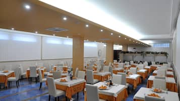 Um salão de jantar amplo com várias mesas, cada uma coberta por toalhas brancas e centros de mesa laranja.