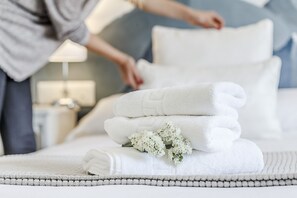 Uma pilha organizada de toalhas brancas com um pequeno arranjo de flores brancas sobre uma cama.