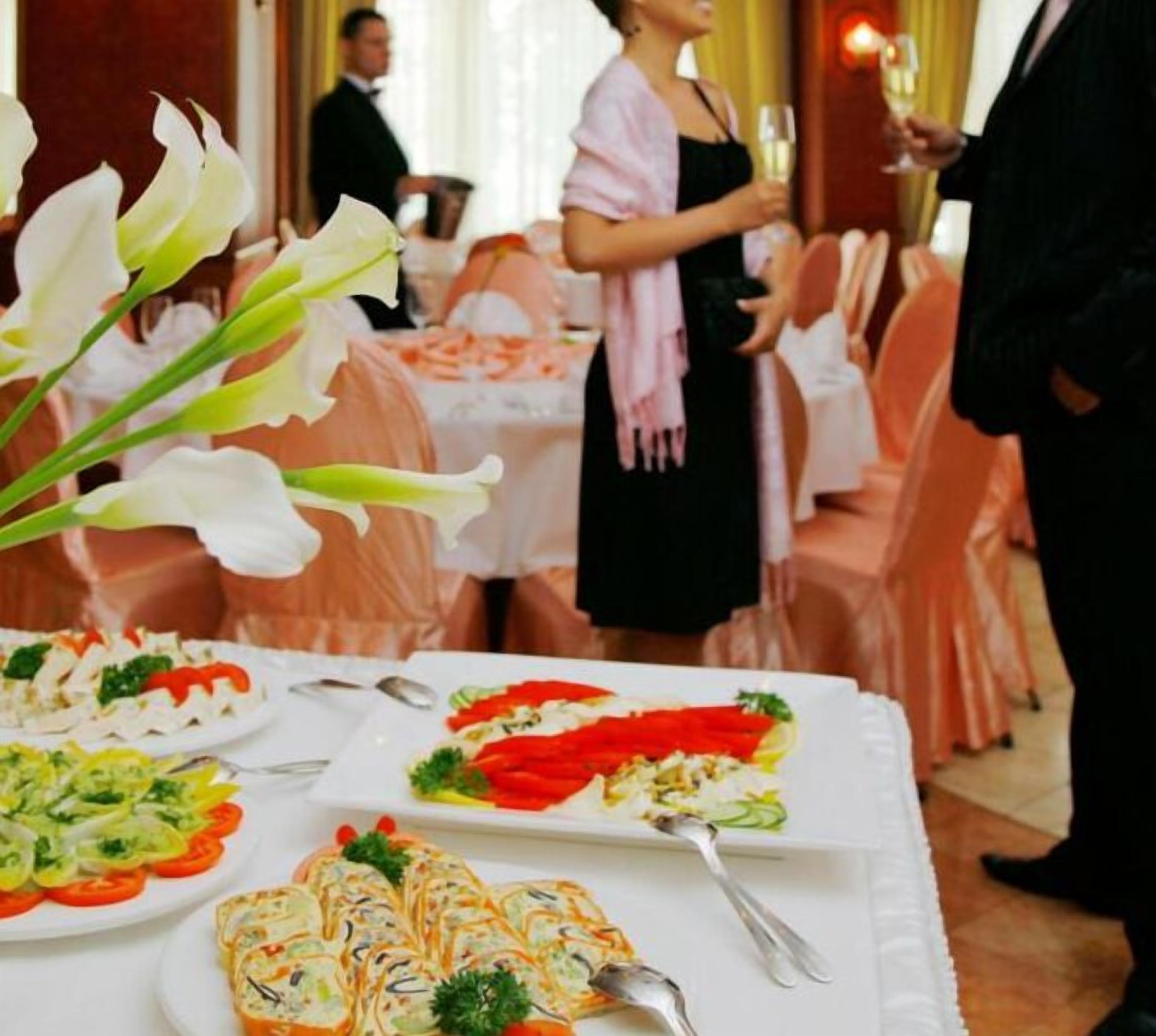 Mesa formal para jantar com toalhas brancas, pratos de comida organizados e um arranjo floral.