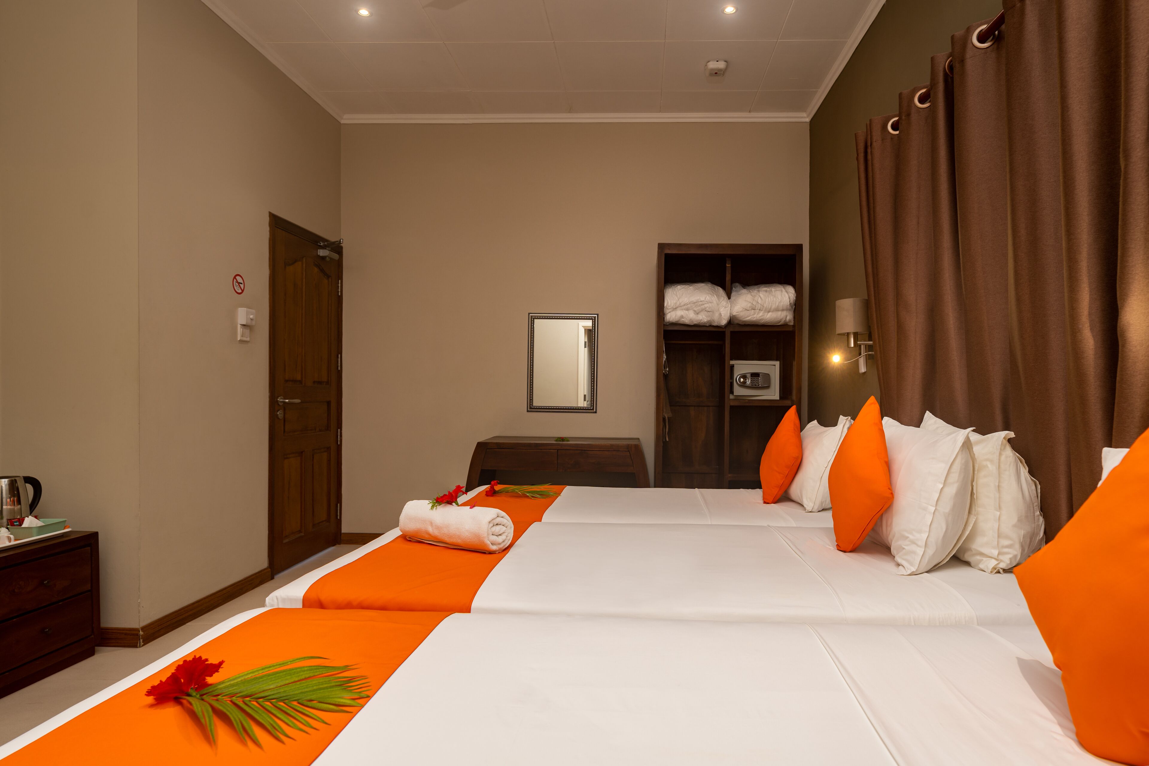 Quarto de hotel com uma cama grande, um guarda-roupa de madeira, um espelho e uma mesa de cabeceira com abajur.