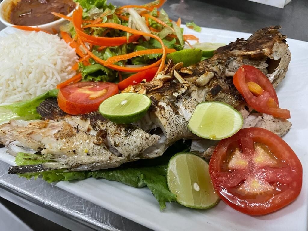 Um prato de peixe grelhado com arroz, salada e rodelas de limão.