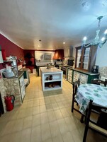 Uma cozinha compacta com uma ilha central, uma área de refeições com mesa, e uma parede vermelha de destaque.