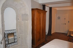 Quarto com arco de pedra, guarda-roupa de madeira, uma cama e uma porta com painel decorativo.