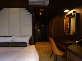 Quarto de hotel com cama, escrivaninha, cadeira e espelho.