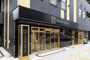 Entrada de hotel com fachada moderna, portas de vidro e uma placa indicando 'KOKO HOTEL'.