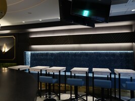 Uma área de bar moderna com um assento acolchoado azul, vários bancos e uma TV de tela plana montada no teto.