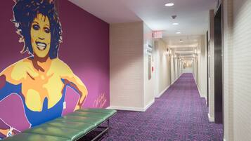 Corredor de hotel com carpete roxo, um banco verde e um mural grande na parede esquerda.