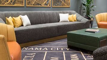 Uma sala de estar moderna com um sofá cinza, almofadas amarelas e brancas, um banquinho verde e um tapete com tema de cidade.