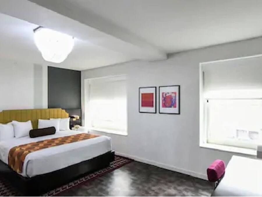 Quarto de hotel moderno com uma cama grande, mesas de cabeceira, escrivaninha e televisão.