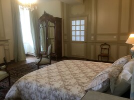 Quarto com cama grande, armário de madeira, uma cadeira, janela e um lustre.
