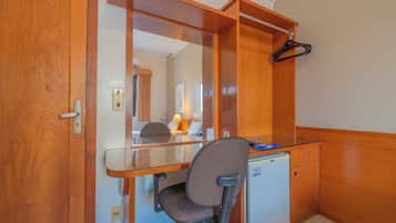 Quarto compacto com guarda-roupa de madeira, escrivaninha, cadeira e um pequeno frigorífico.