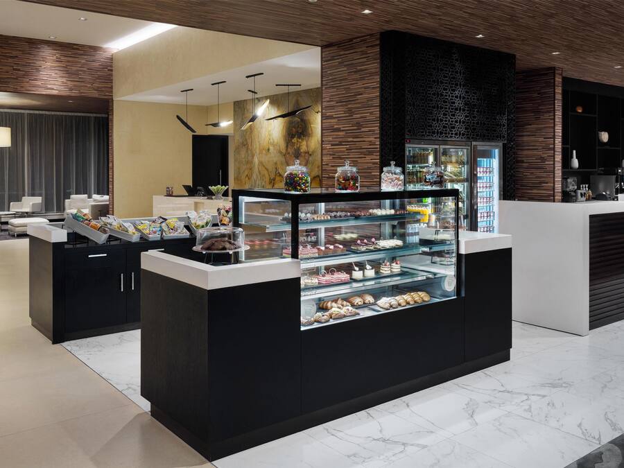Um lobby de hotel moderno com um balcão de recepção, área de estar e uma mesa central para sobremesas.