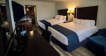 Quarto de hotel com duas camas, uma escrivaninha, uma máquina de café e uma televisão.